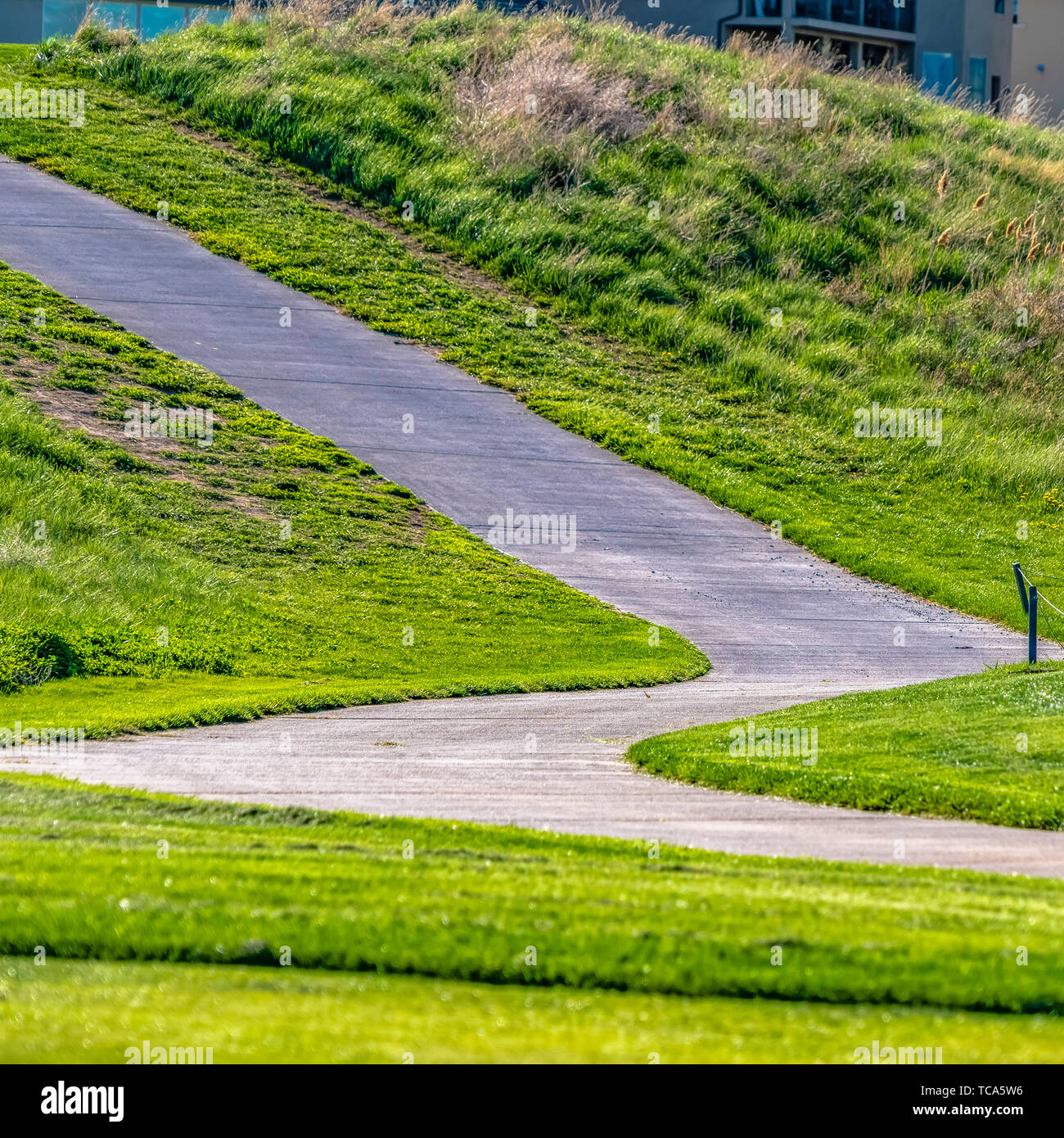 Square Paved road that runs on a hill with rich green grasses viewed on ...