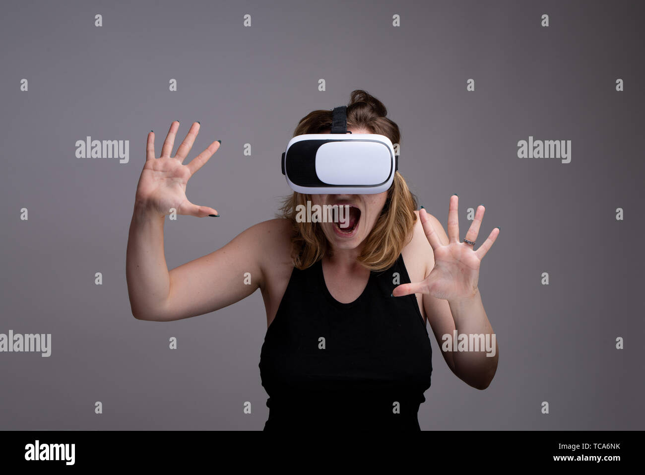 Young female using 3D VR gadget is displaying a terrified and shocked ...