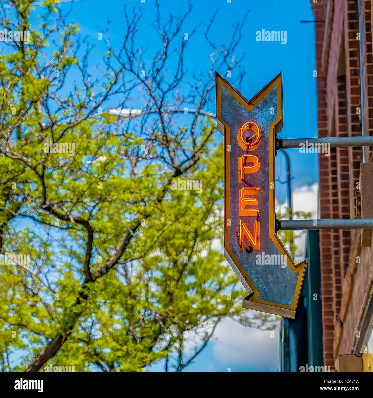 Frame Square Open arrow sign on a building with vibrant trees and blue ...