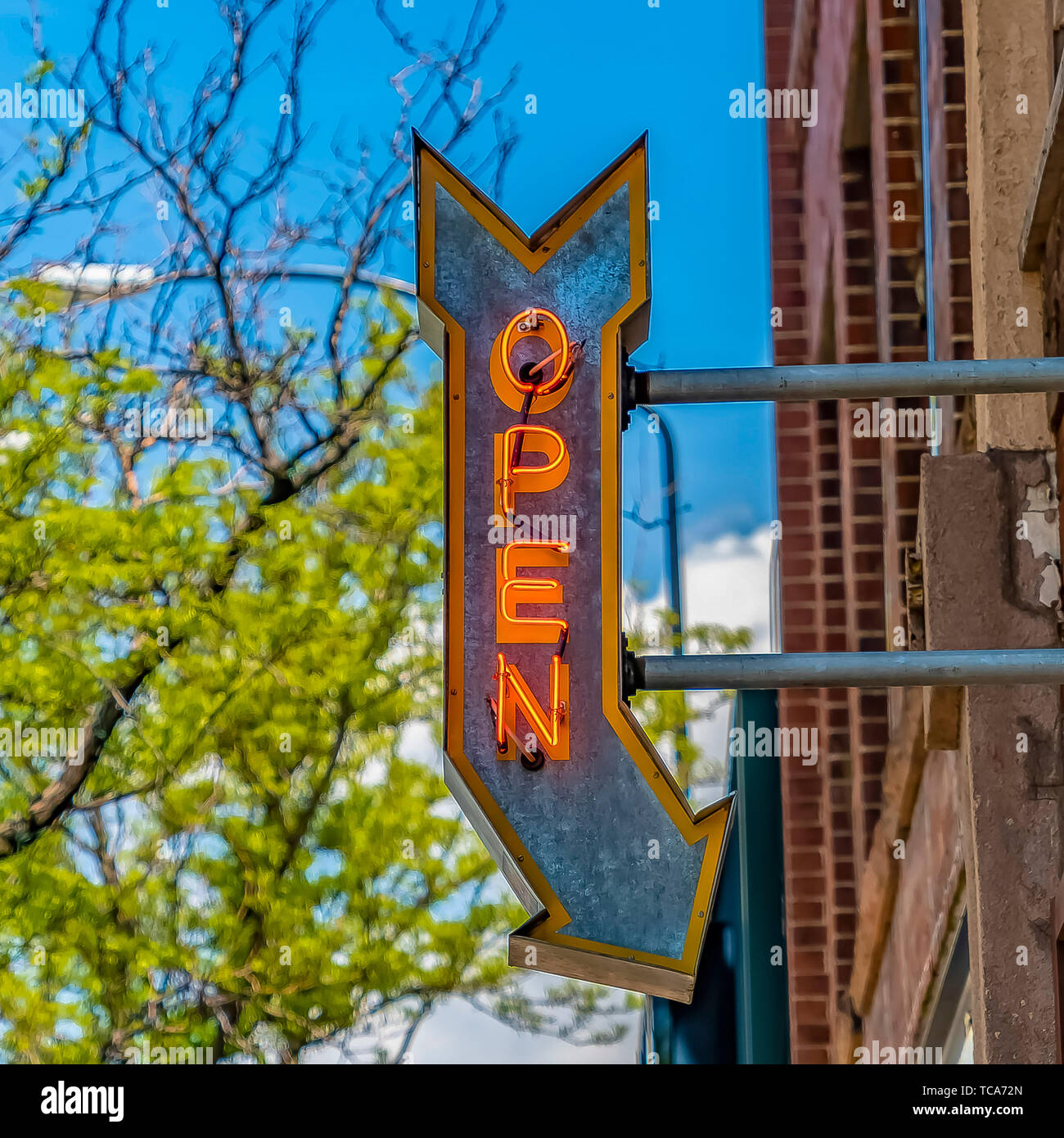 Square Open arrow sign on a building with vibrant trees and blue sky in ...