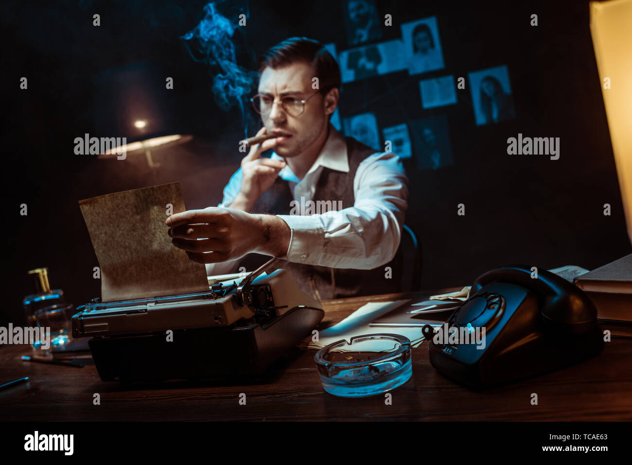 Detective in glasses smoking cigar while using typewriter in dark ...