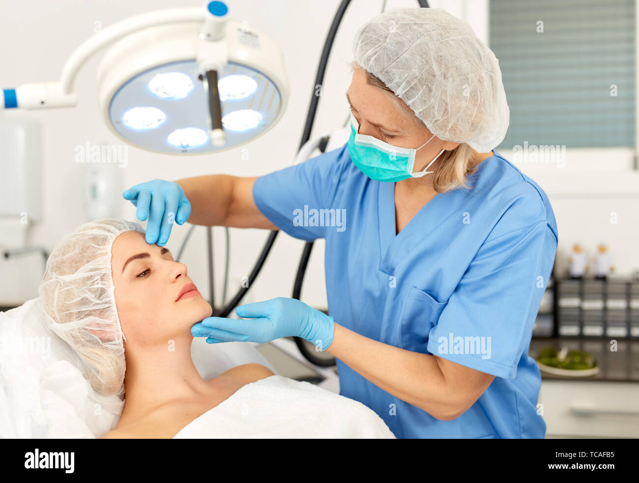 Professional cosmetician examining face skin of girl in clinic of ...