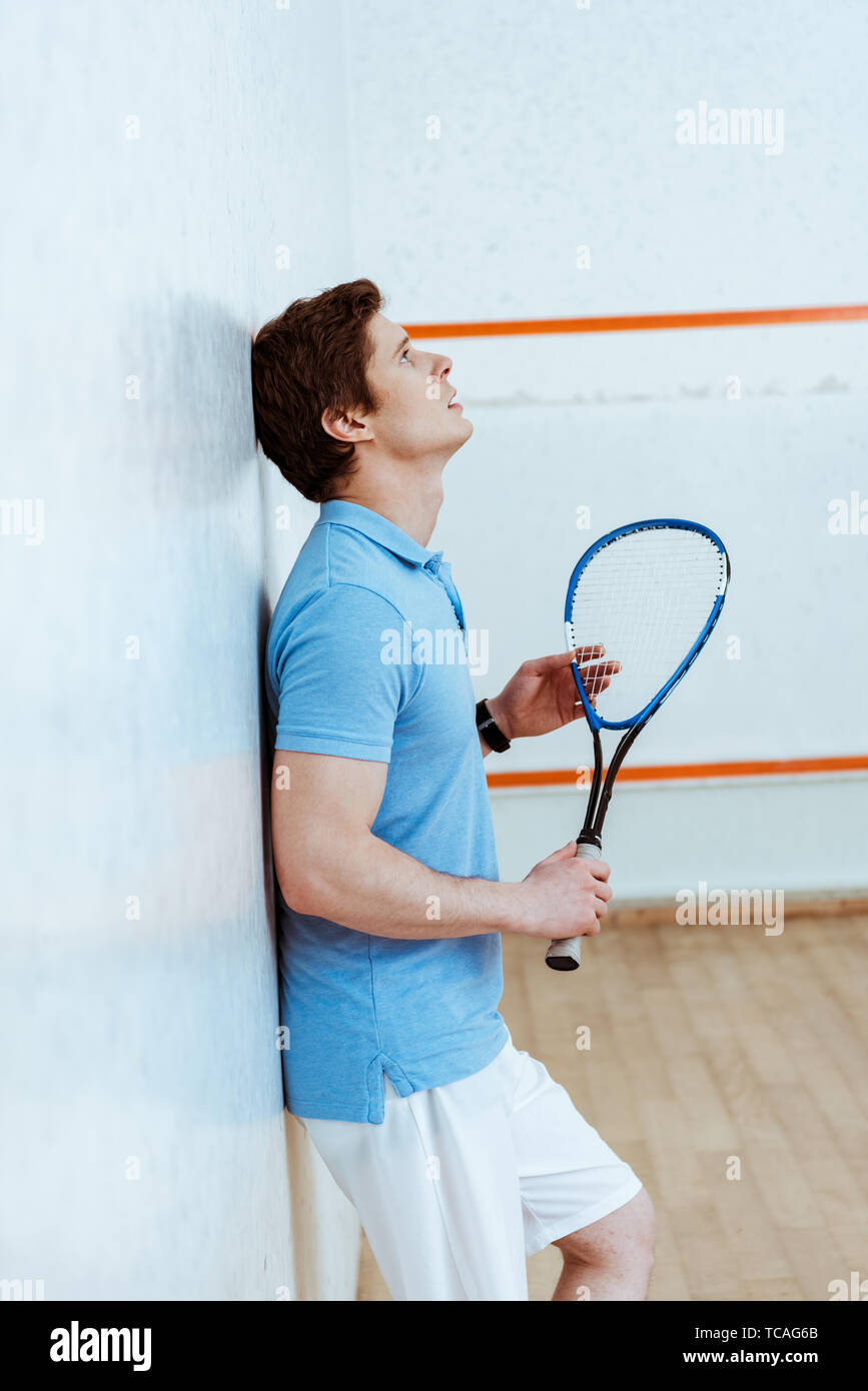 Side view of sad squash player holding racket in four-walled court ...