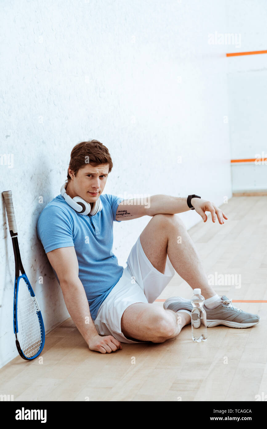 Sad squash player in blue polo shirt sitting on floor and looking at ...