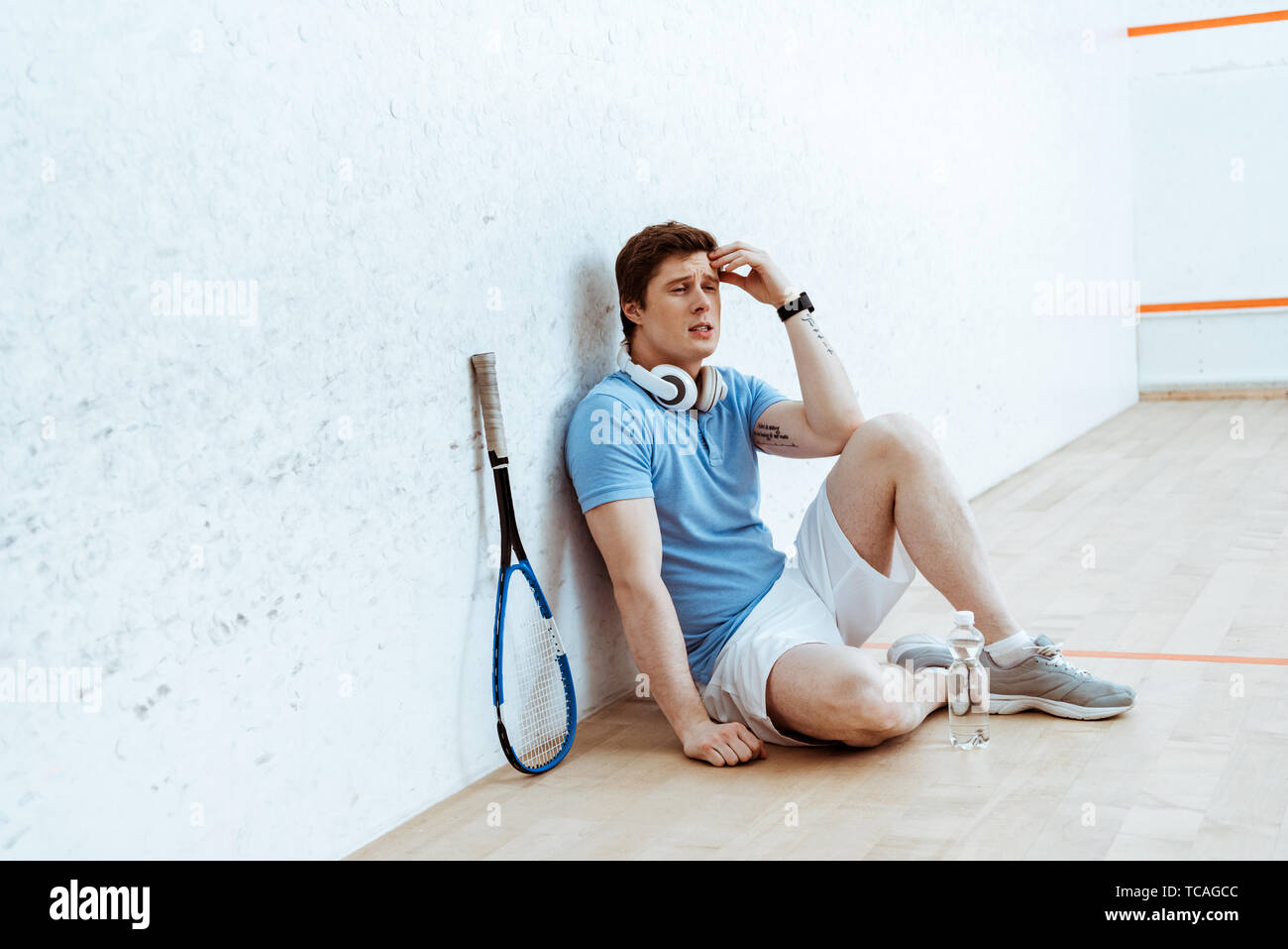 Sad squash player in blue polo shirt sitting on floor and looking away ...