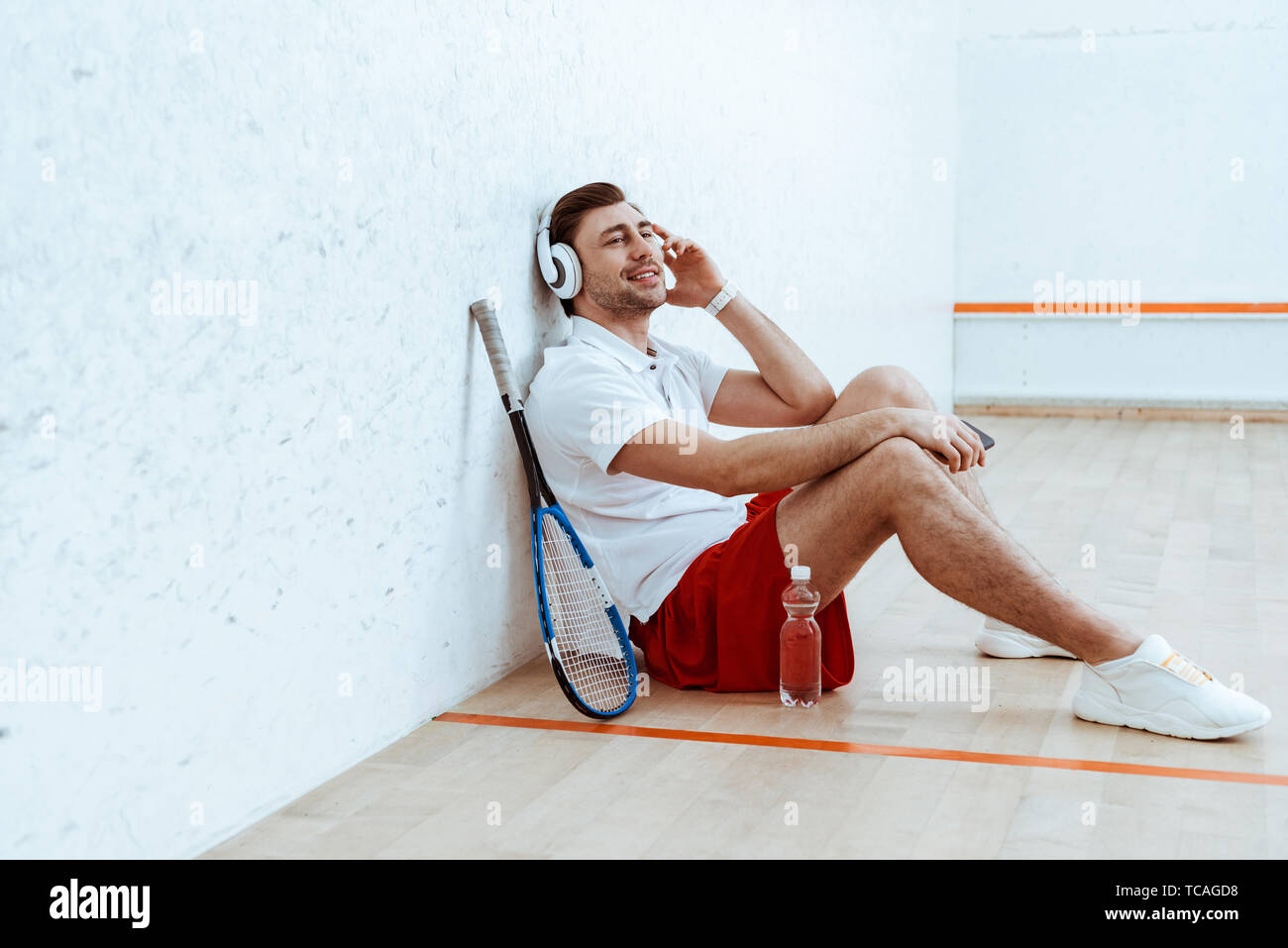 Smiling squash player sitting on floor and listening music in ...