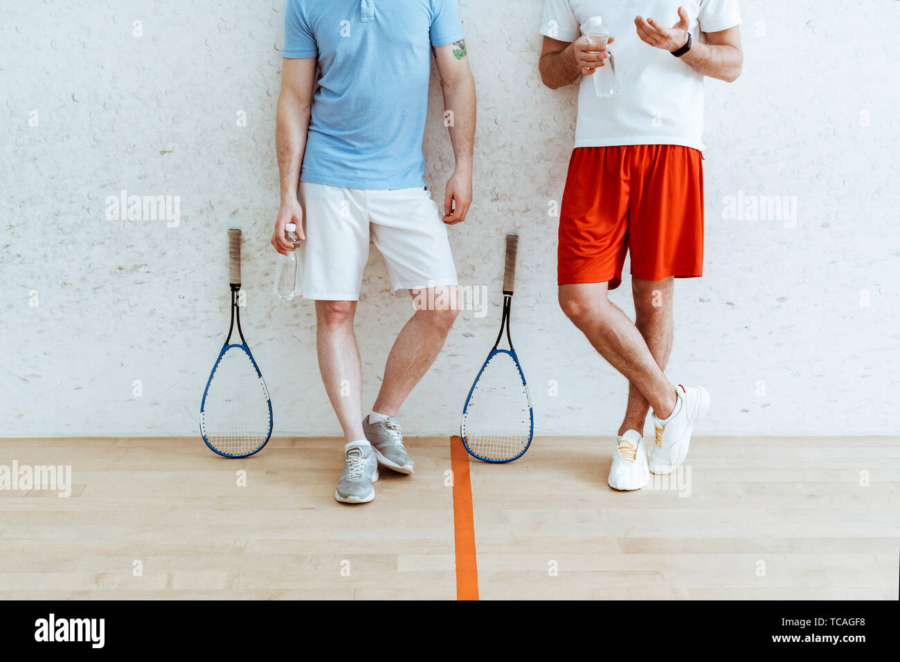 Cropped view of two squash players in shorts standing with crossed legs ...