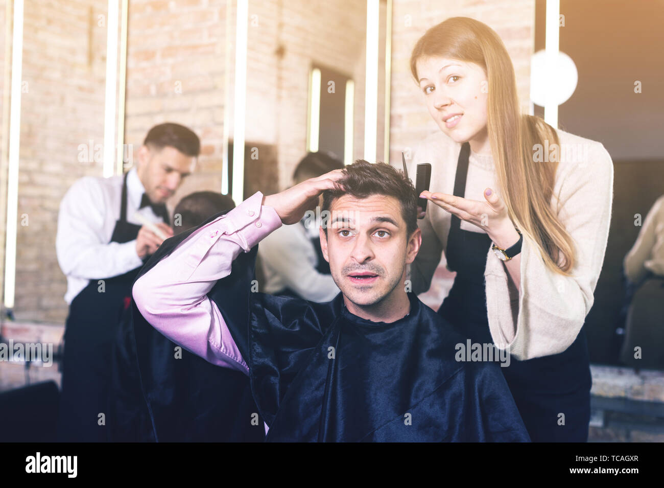 Portrait of shocked man with apologetic female hairdresser at ...
