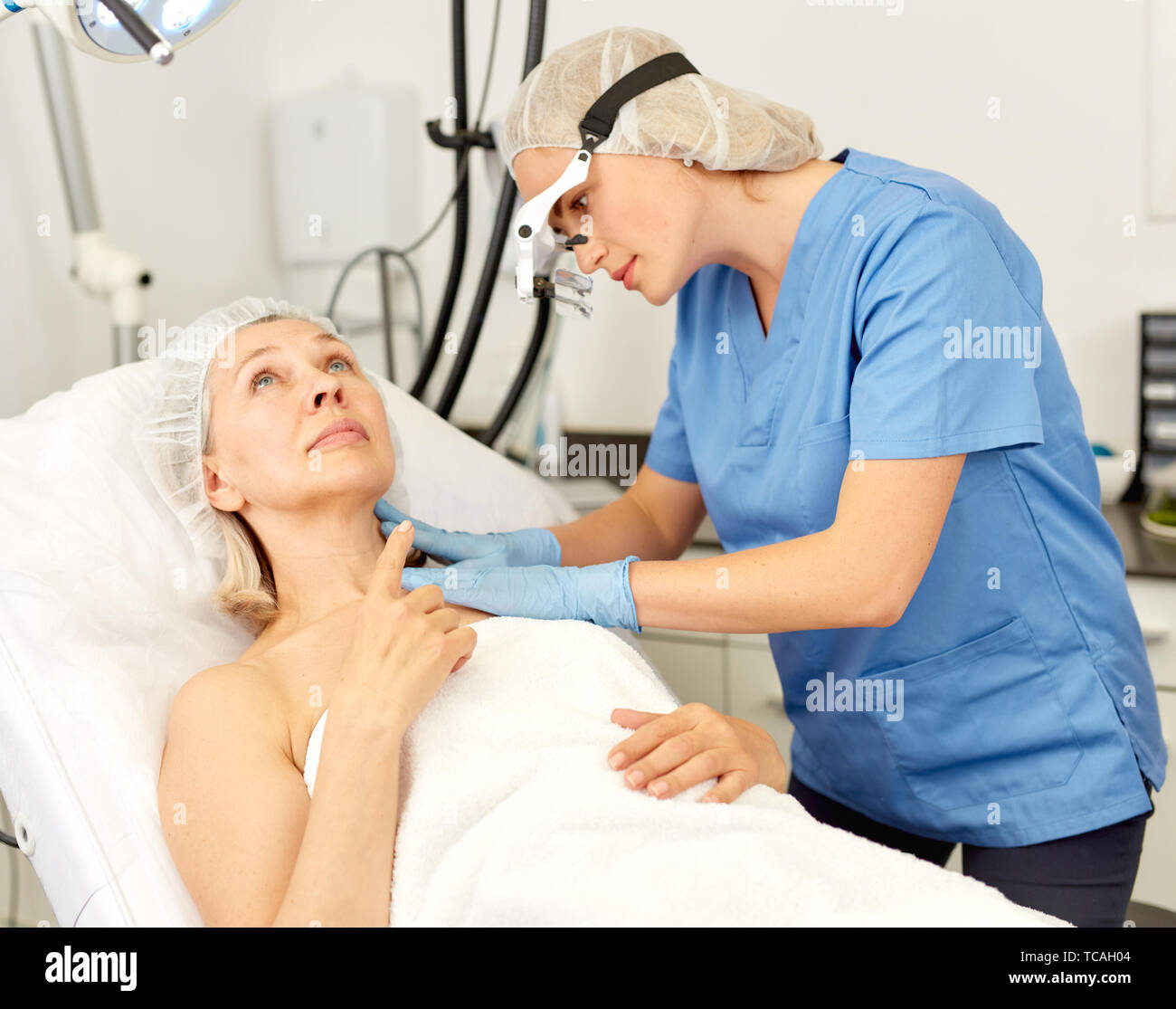 Professional cosmetician examining face skin of mature woman in clinic ...