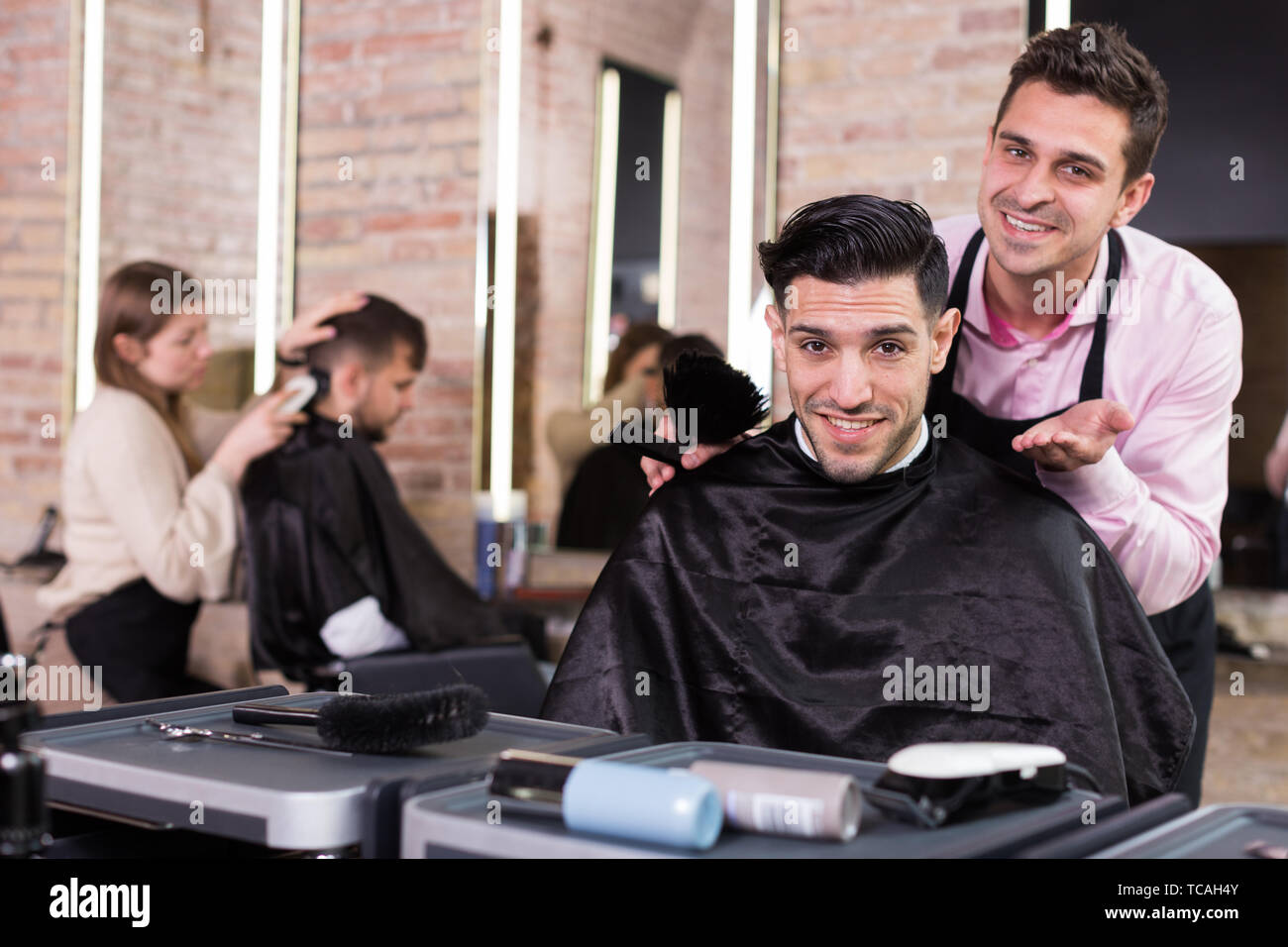 Skillful hairdresser finished haircut and showing result to pleased man ...