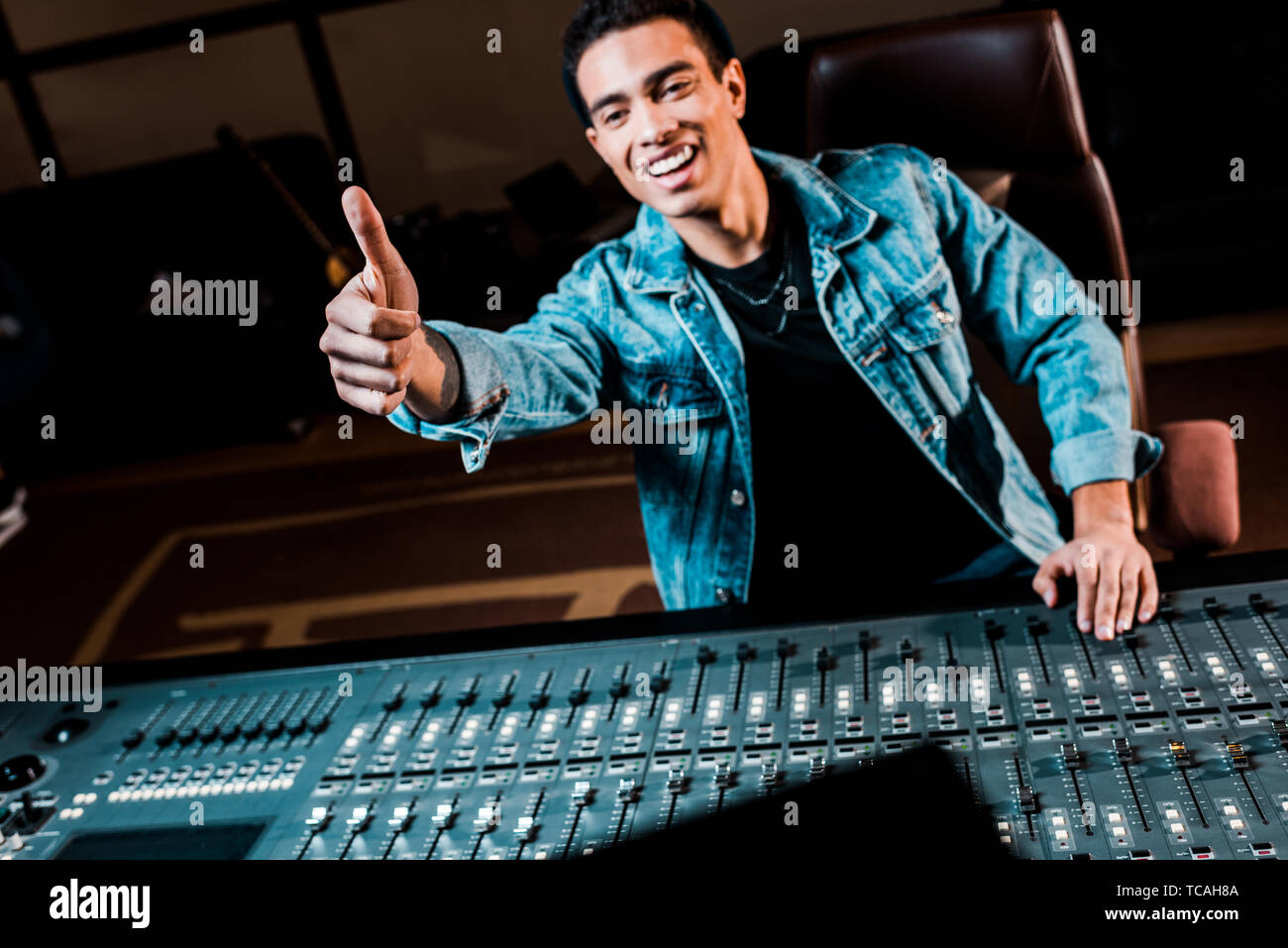 smiling mixed race sound producer showing thumb up while standing near ...