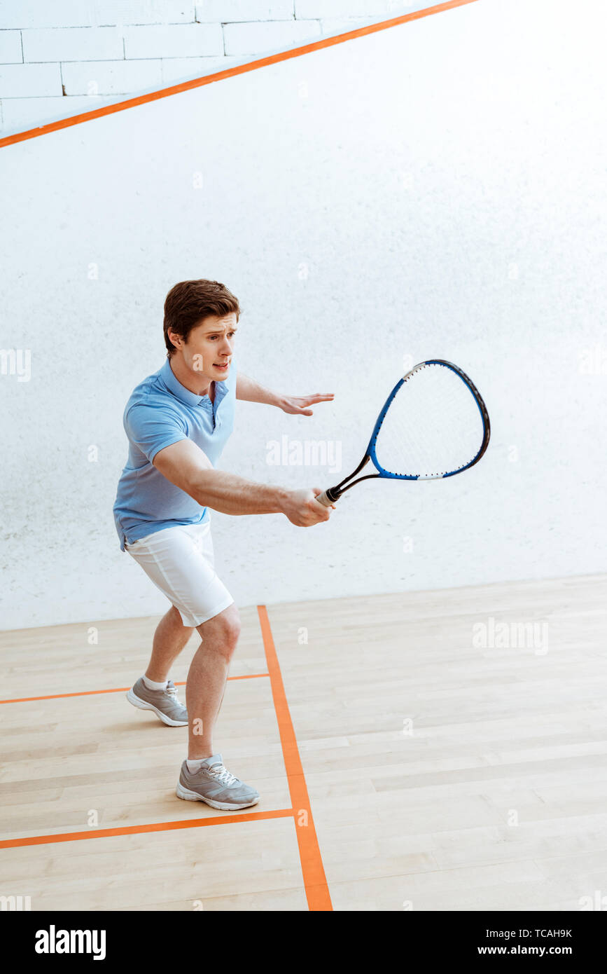 Emotional sportsman in blue polo shirt playing squash in four-walled ...