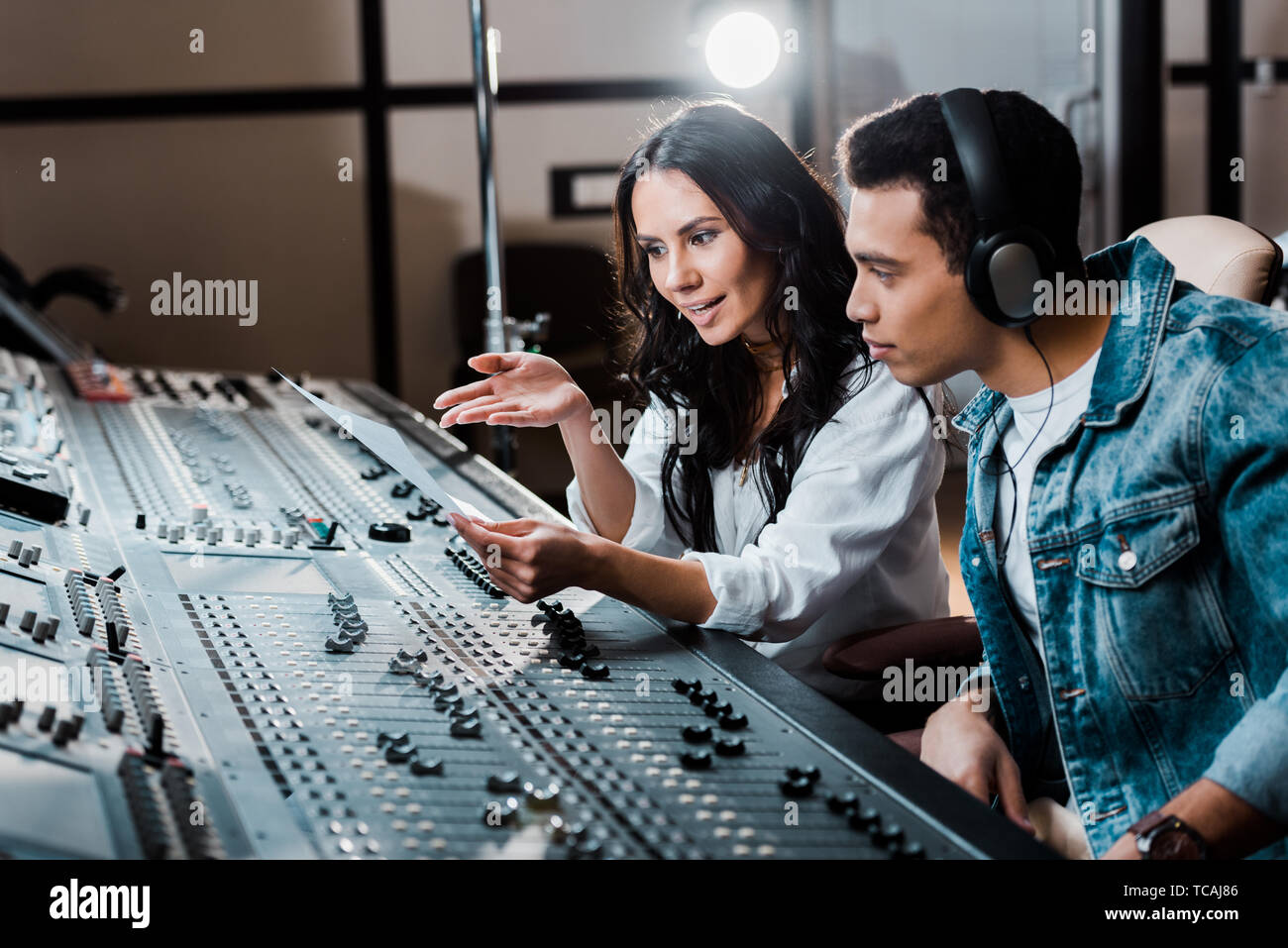 two young multicultural sound producers working at mixing console in ...