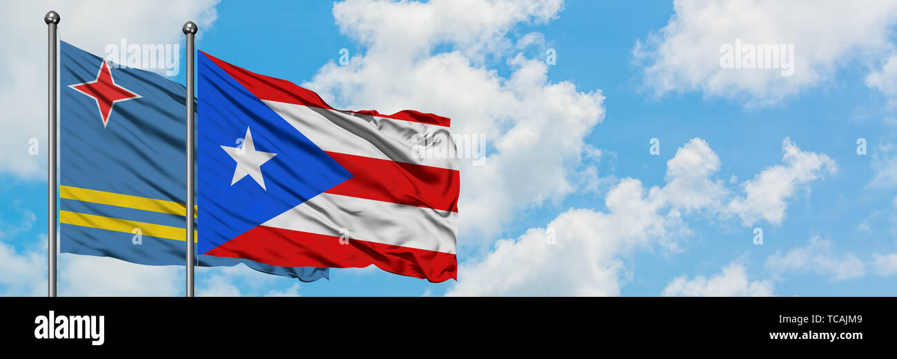 Aruba and Puerto Rico flag waving in the wind against white cloudy blue ...