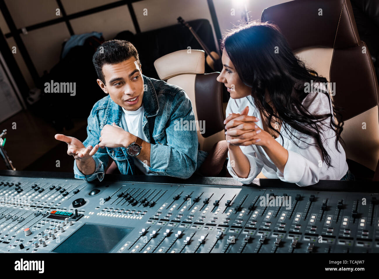 two smiling multicultural sound producers talking while sitting near ...