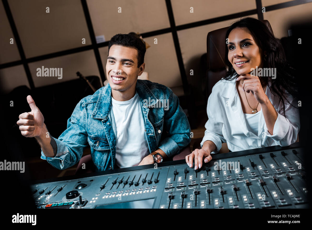 handsome multicultural sound producer showing thumb up while sitting ...