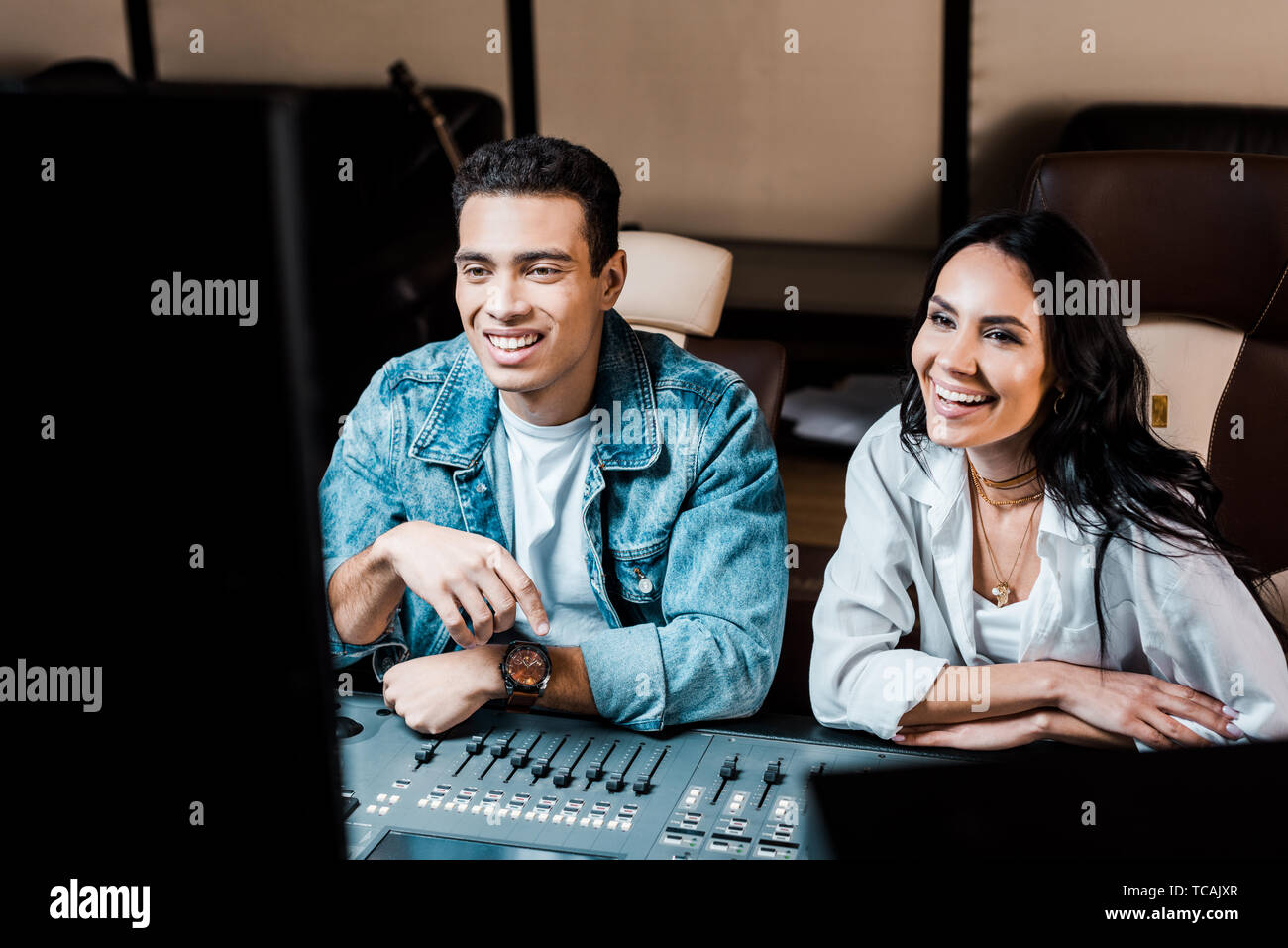 two cheerful multicultural sound producers working at mixing console in ...
