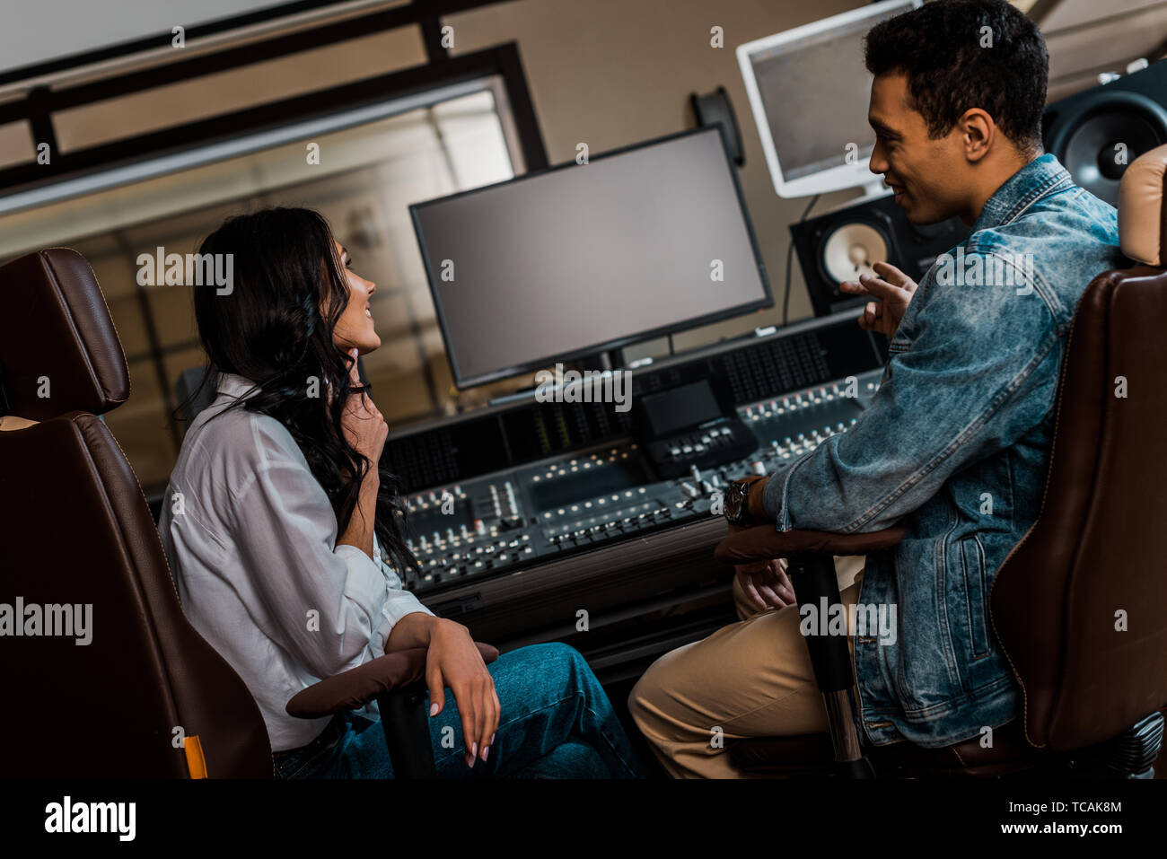 two young smiling sound producers working sitting near mixing console ...