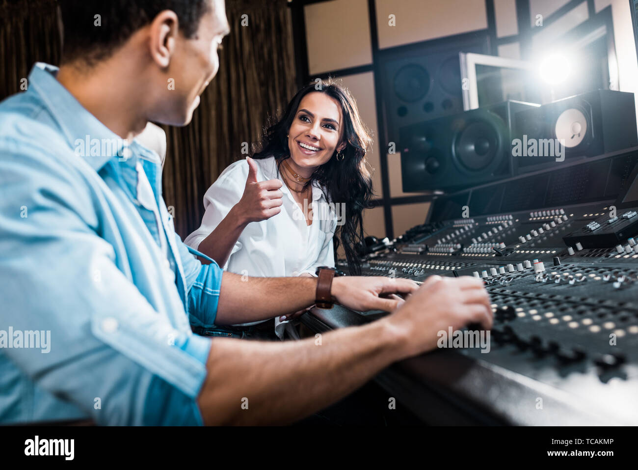 selective focus of pretty sound producer showing thumb up near handsome ...