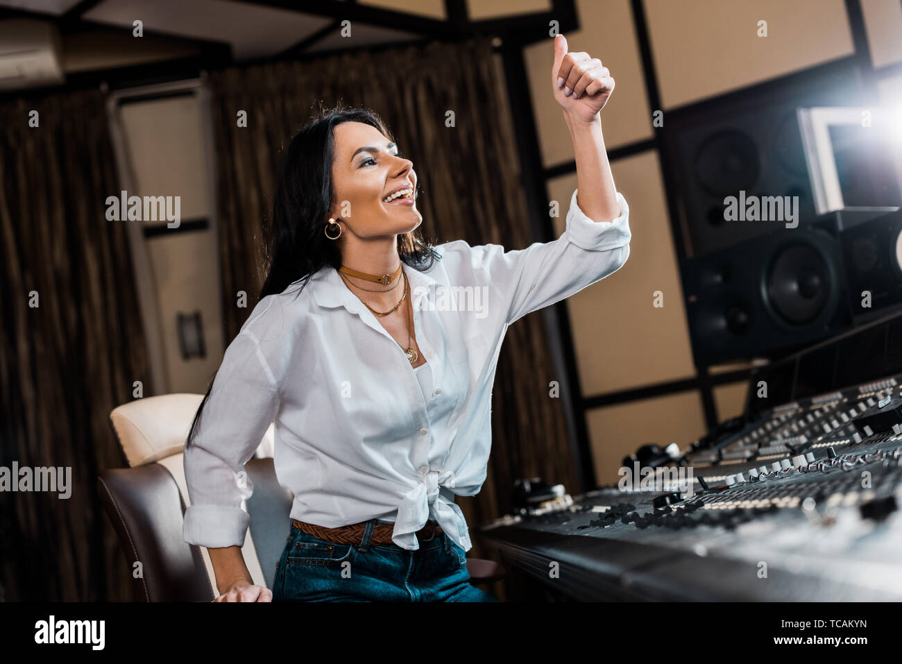 selective focus of pretty sound producer showing thumb up in recording ...