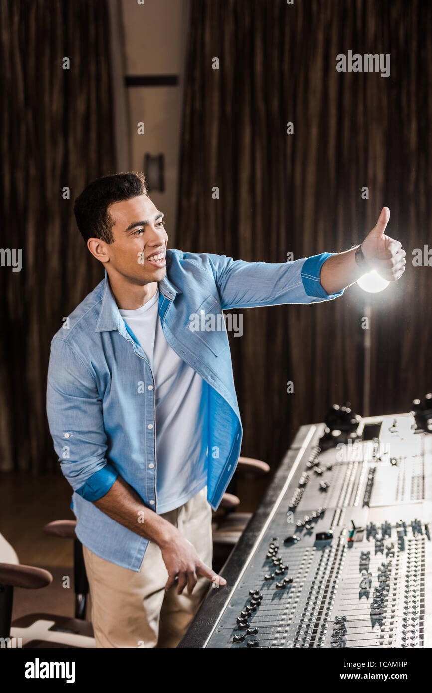 cheerful mixed race sound producer showing thumb up while working at ...