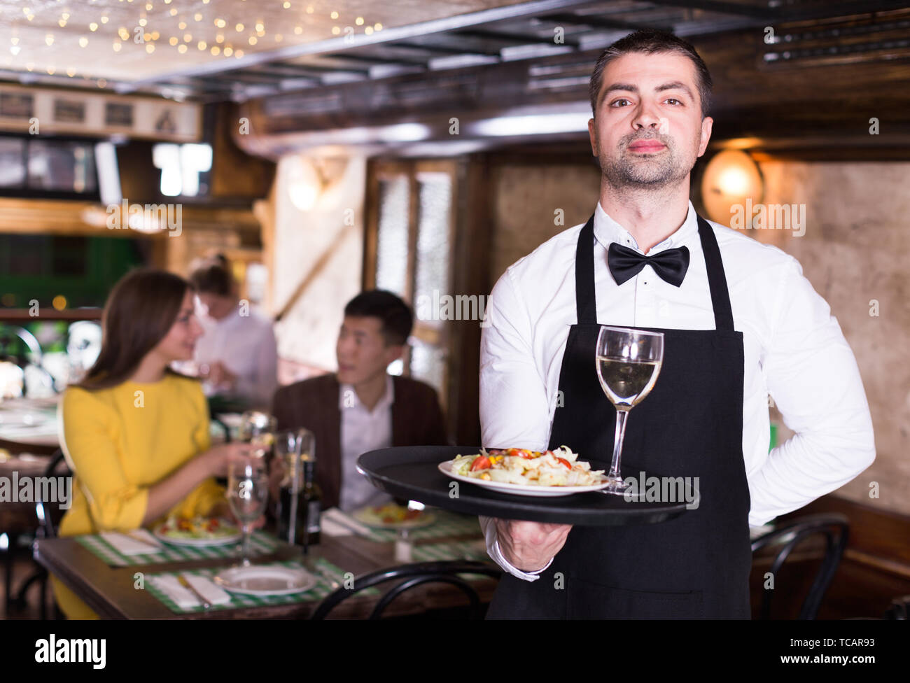 Portrait of male waiter who is holding tray with order in hall of ...