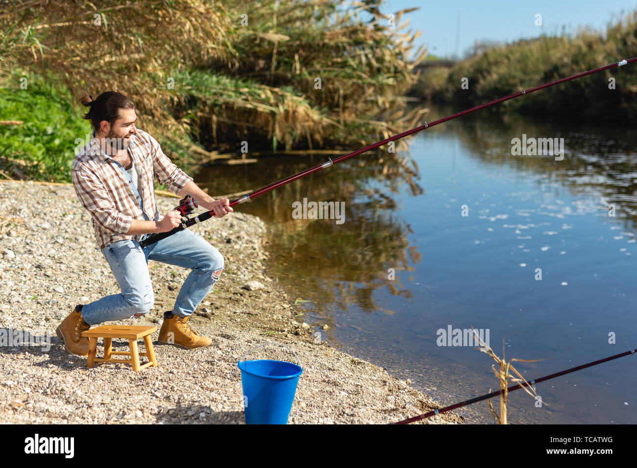 Adult man standing near river and pulling fish expressing emotions of ...