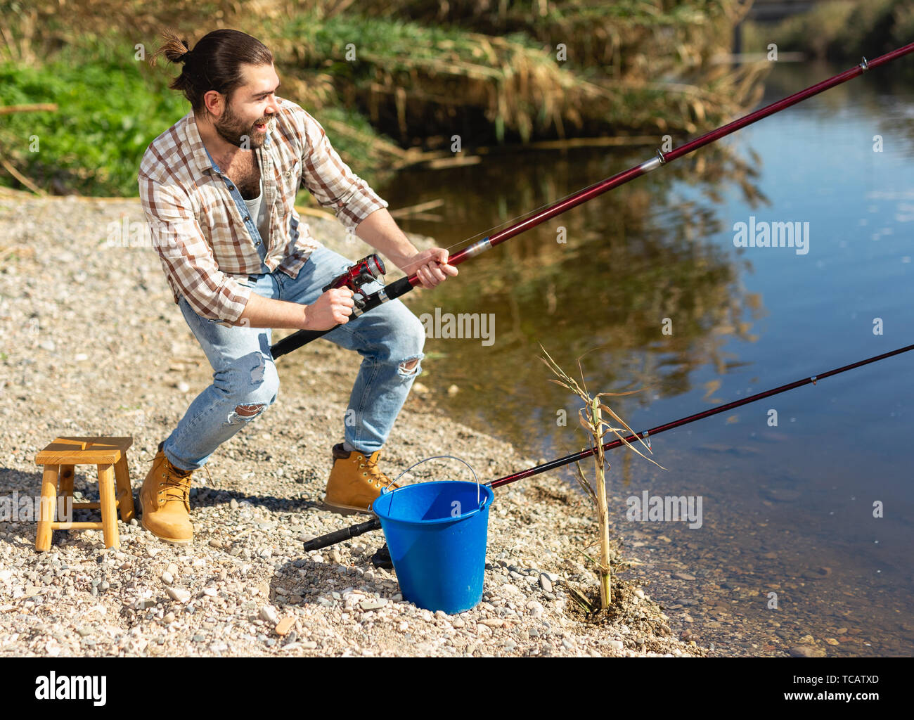 Adult man standing near river and pulling fish expressing emotions of ...
