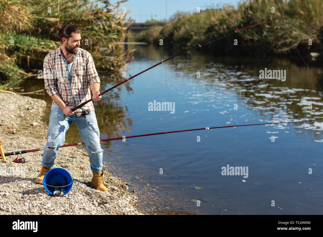 Adult man standing near river and pulling fish expressing emotions of ...