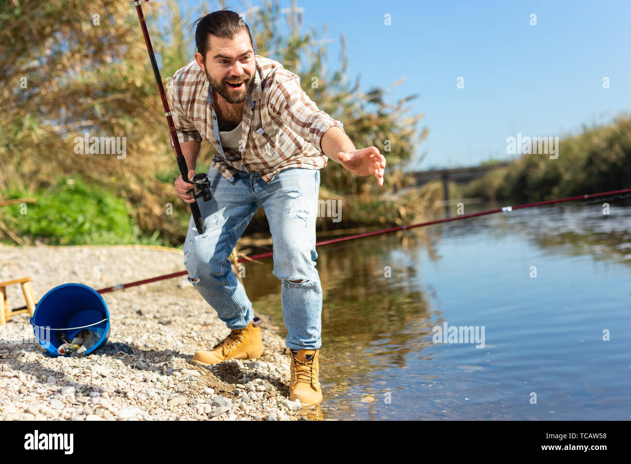 Adult man standing near river and pulling fish expressing emotions of ...