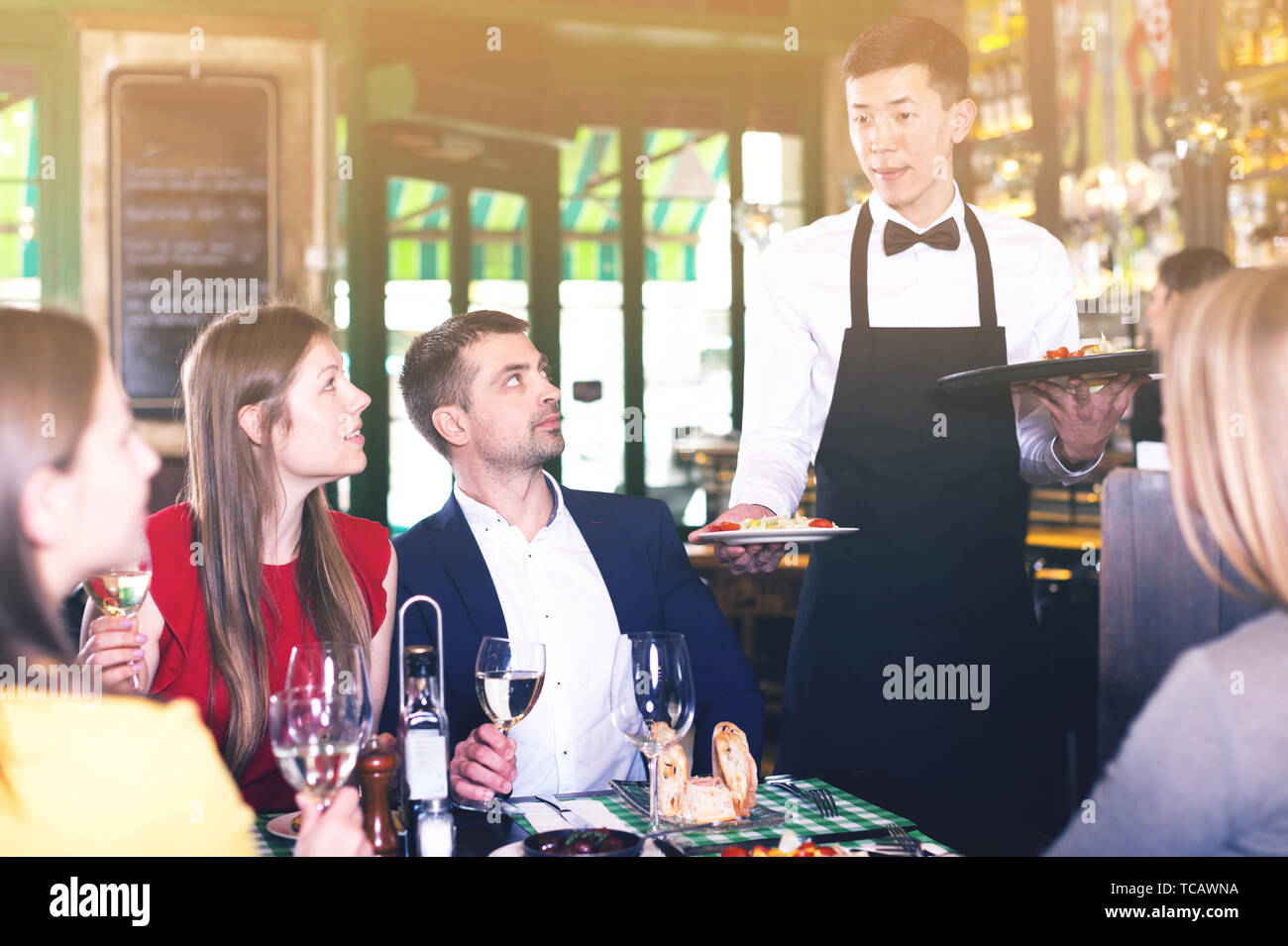 Male waiter is serves an order for smiling friends who are drinking ...