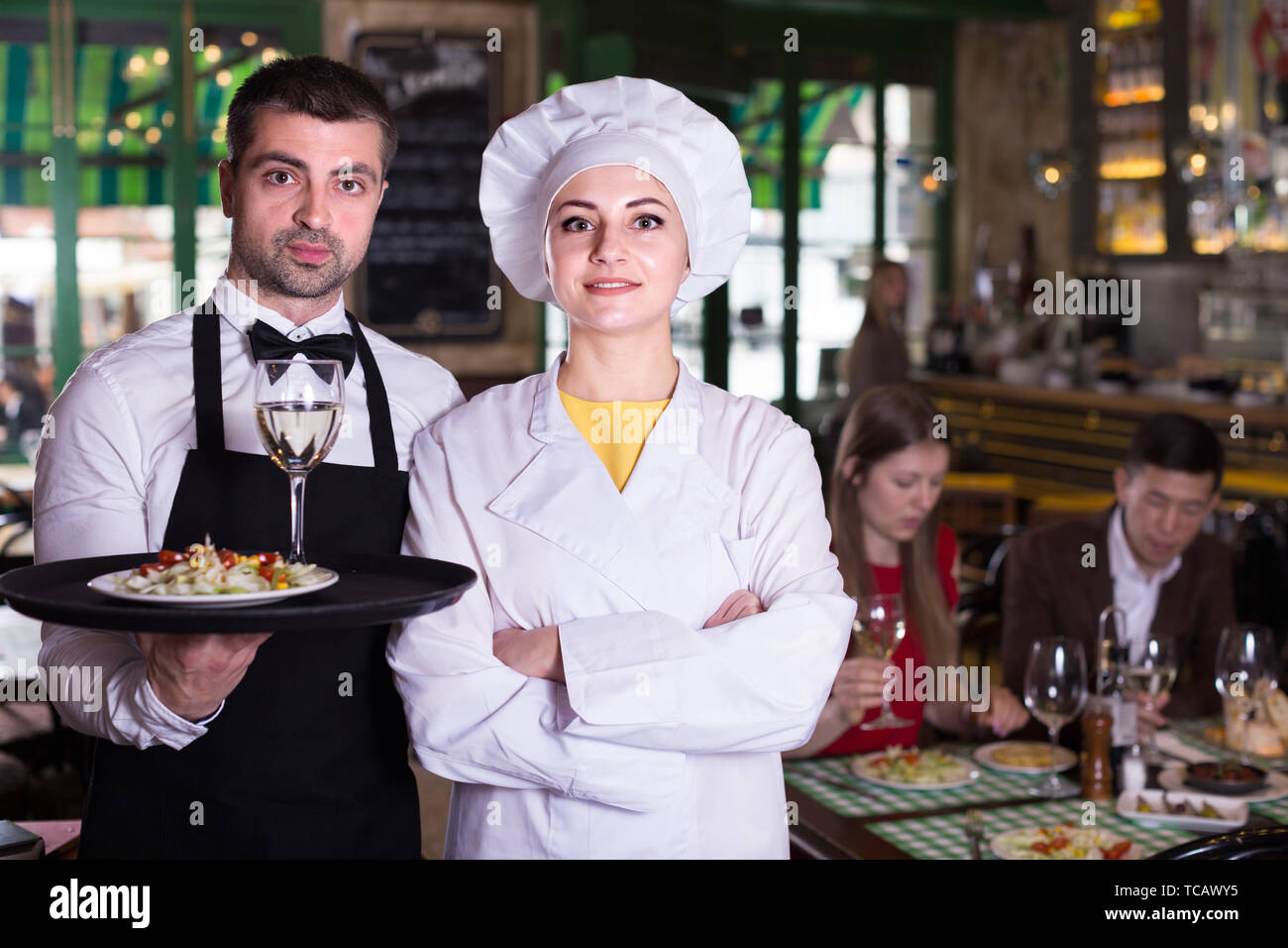 Portrait of male waiter and female cook who are welcoming clients in ...