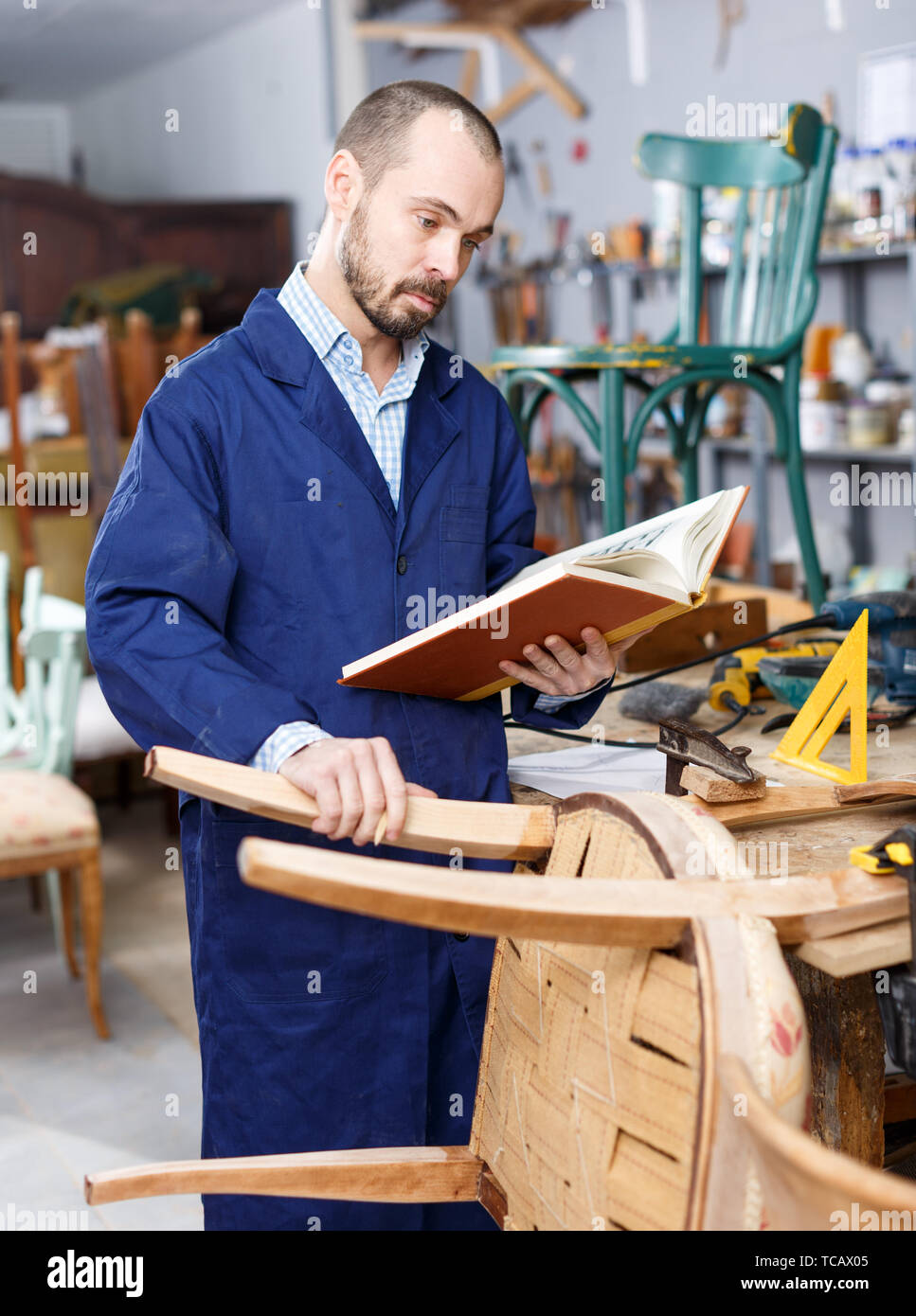 Professional furniture restorer holding album in his hands at woodwork ...
