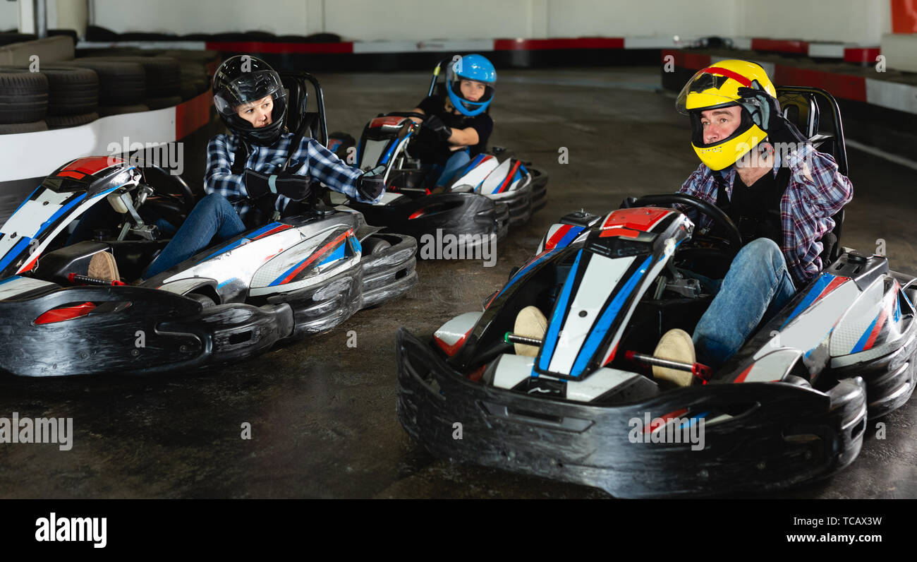 Group of glad male and females in helmets driving racing cars at kart ...