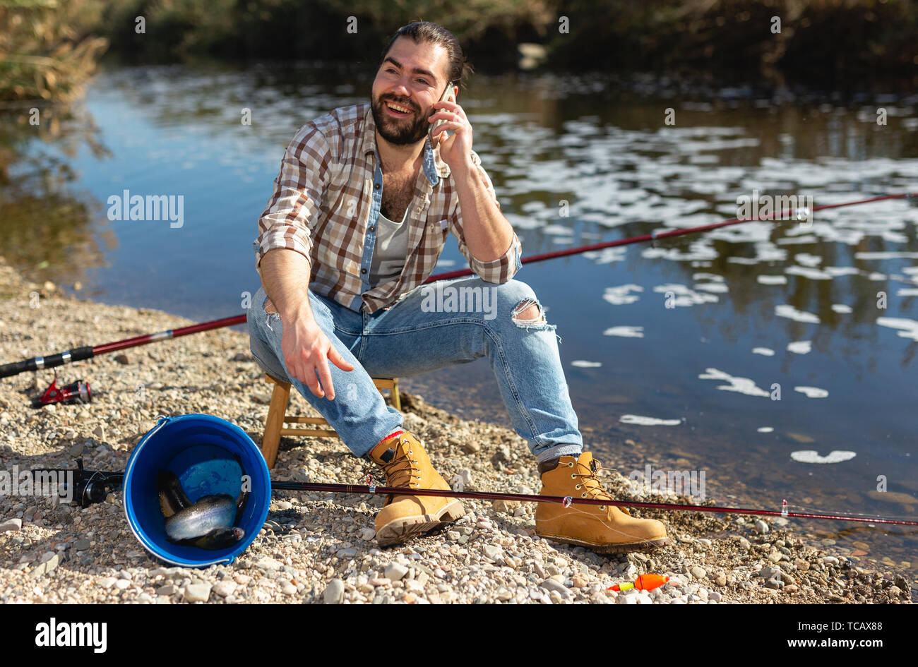 Adult fisherman talking on mobile phone by the river Stock Photo - Alamy