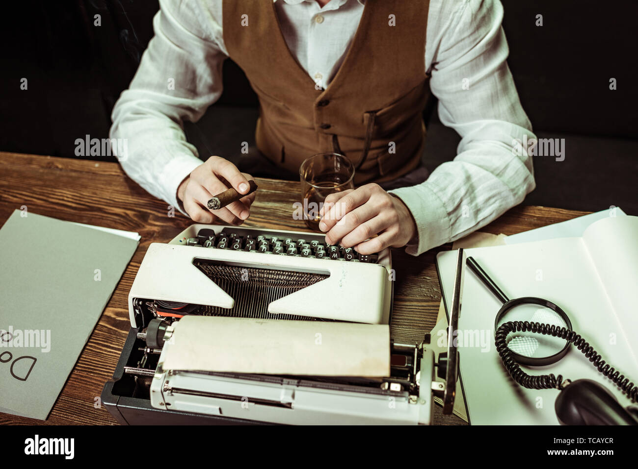 Partial view of detective with cigar using typewriter in office Stock ...