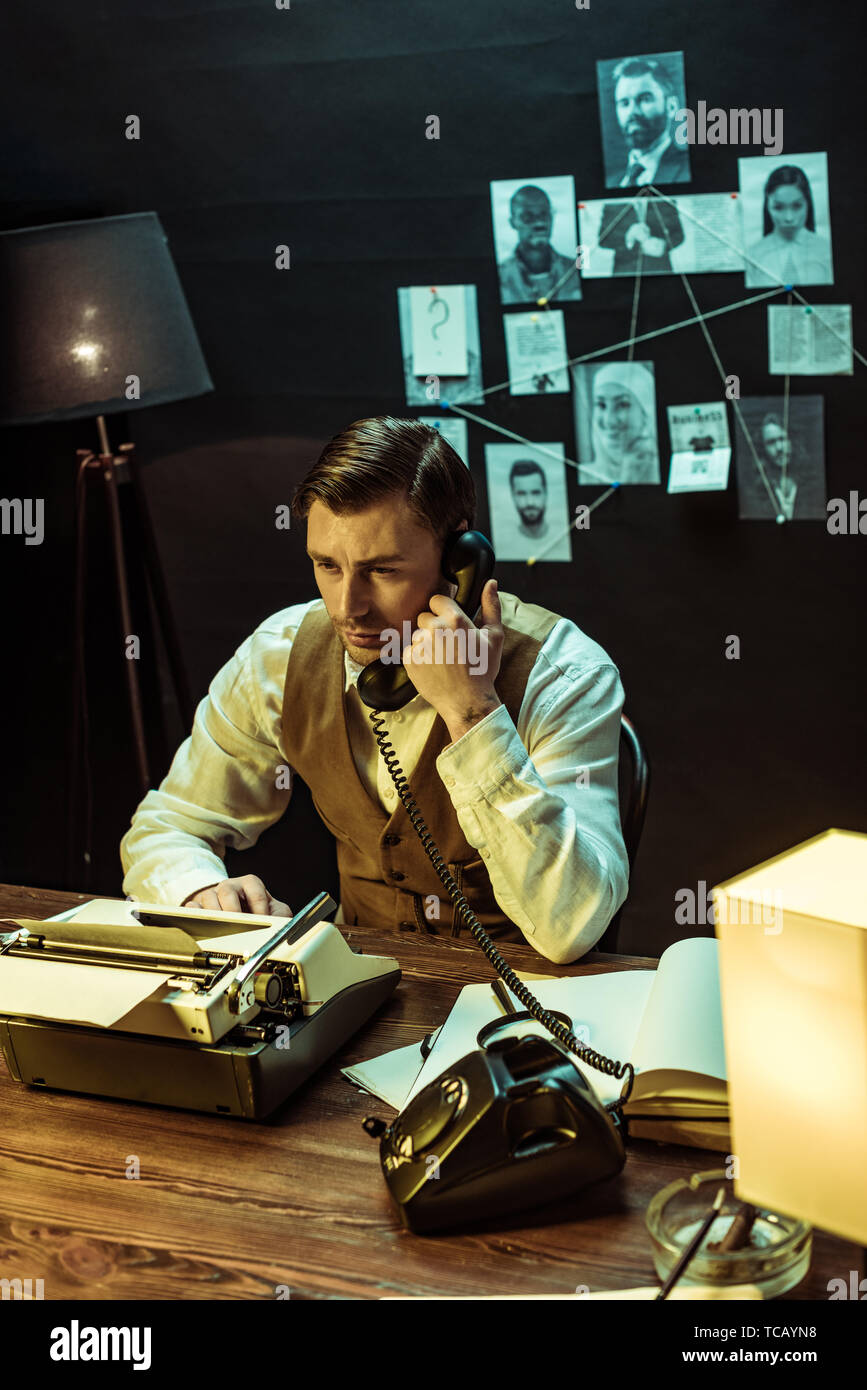 Detective sitting at table with typewriter and talking on telephone in ...