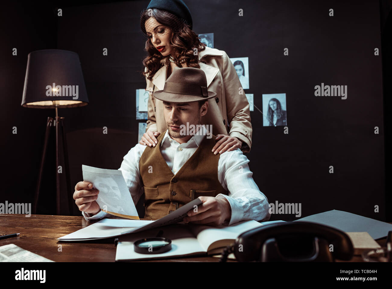 Detective and beautiful woman in trench coat looking at photo in dark ...