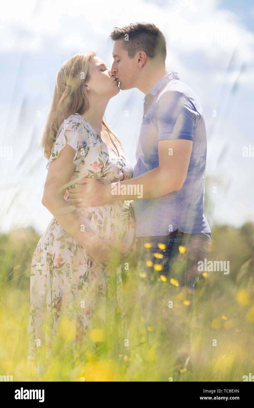 Young happy pregnant couple in love holding hands, relaxing in meadow ...