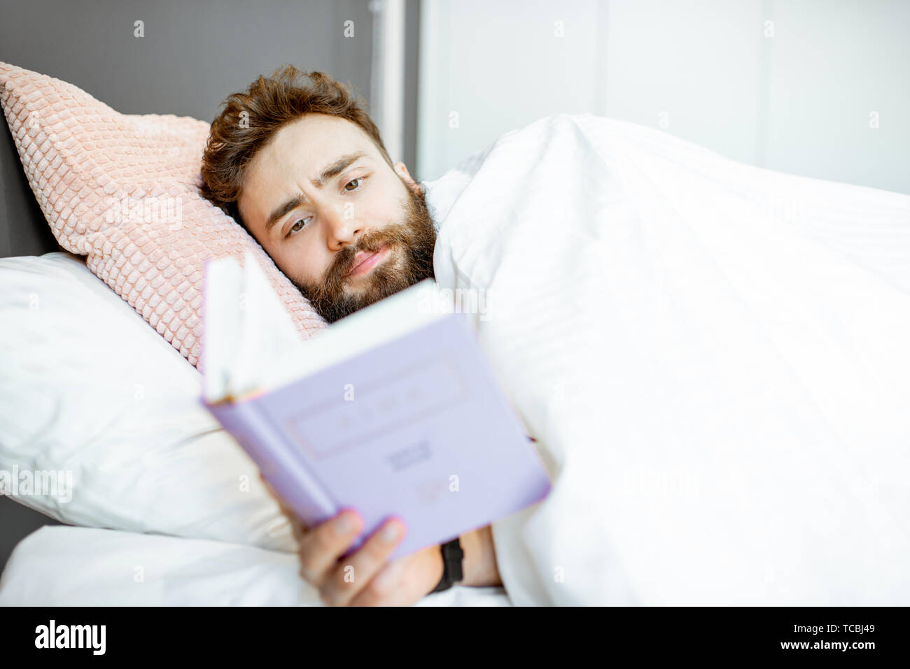 Creative man reading book before the sleep, lying under the white ...