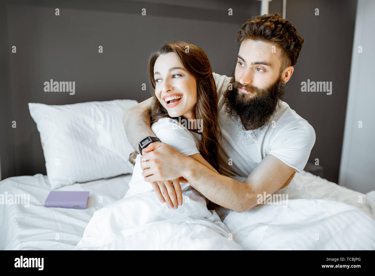 Portrait of a young and happy couple hugging together on the bed at ...