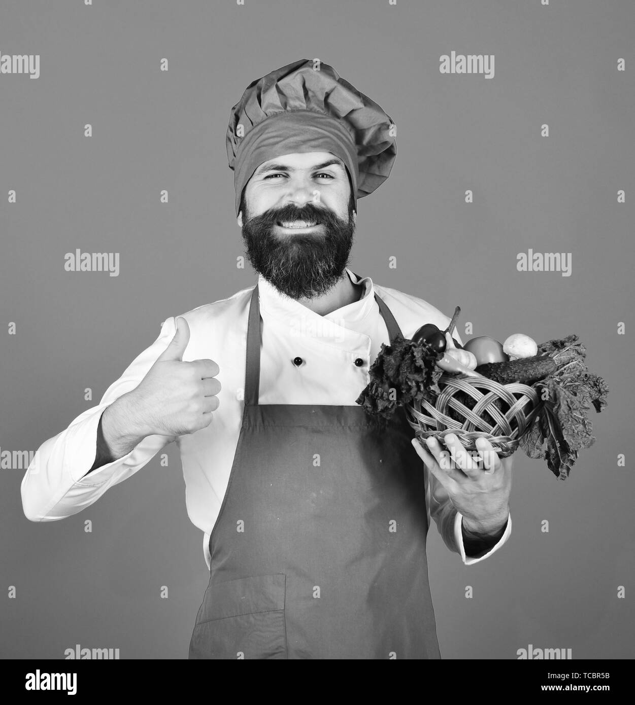 Cook with smile in burgundy uniform holds vegetables in wicker bowl ...