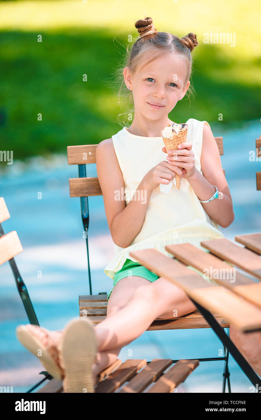 Little girl eating ice-cream at summer in outdoor cafe. Cute kid ...