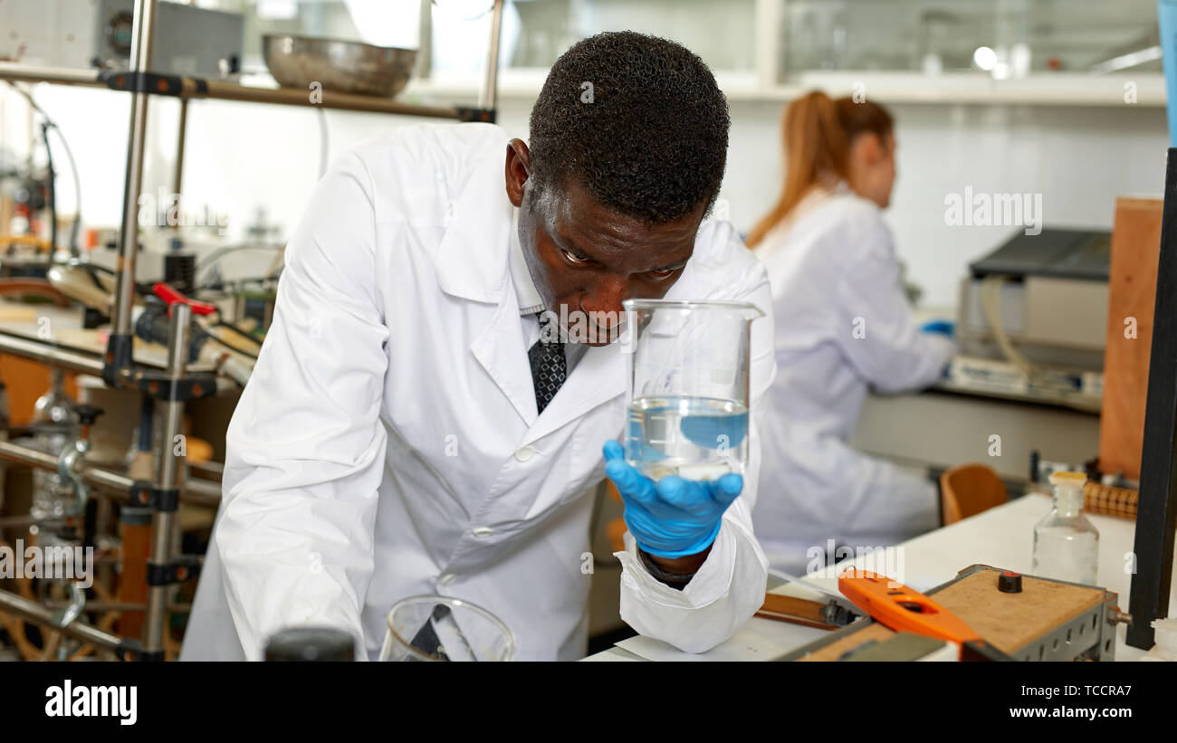 Serious male scientist with test tubes checking for result of chemical ...