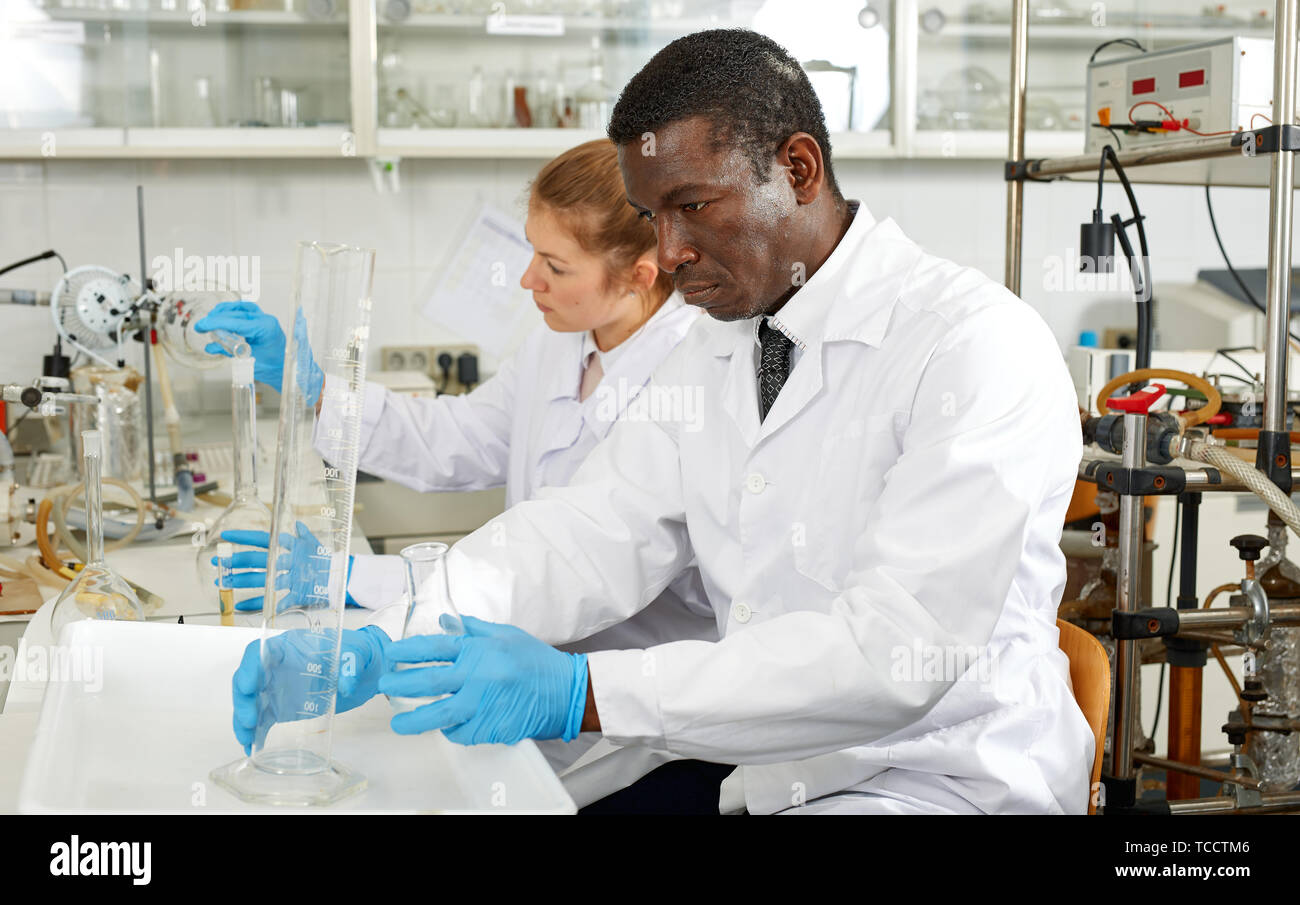 Focused lab technicians in gloves working with glass test tubes before ...