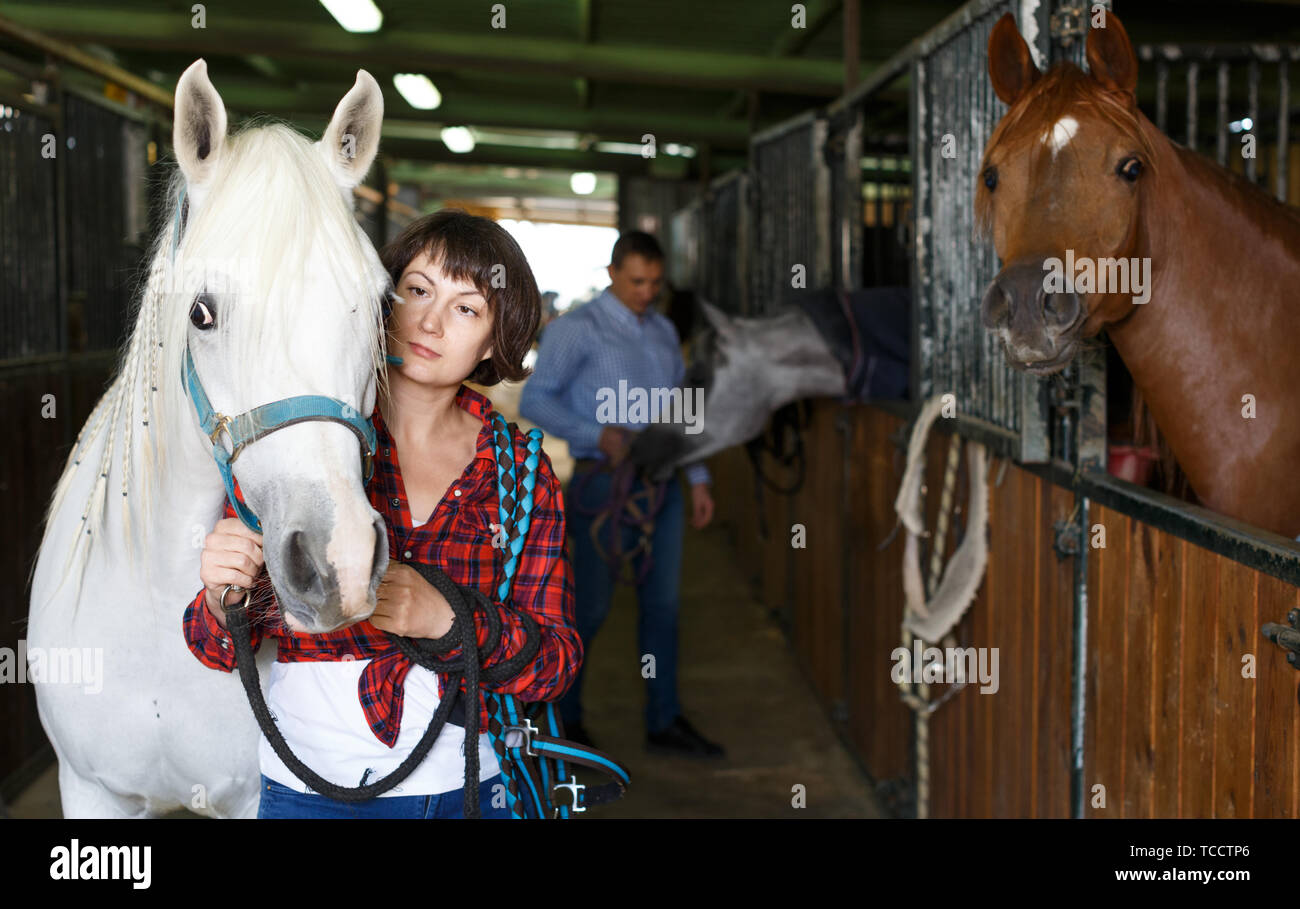 Portrait of cheerful woman horse farm worker standing at stable Stock ...