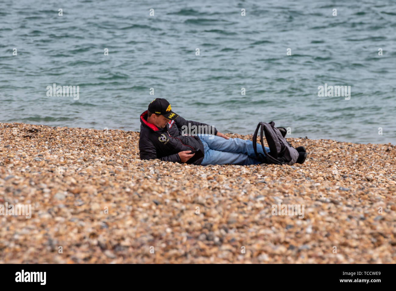 A man laying on a pebble beach using his mobile phone or cell phone ...