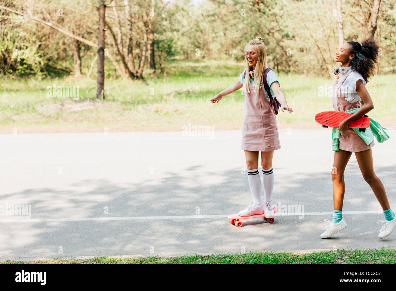 full length view of two multicultural friends skateboarding on road ...