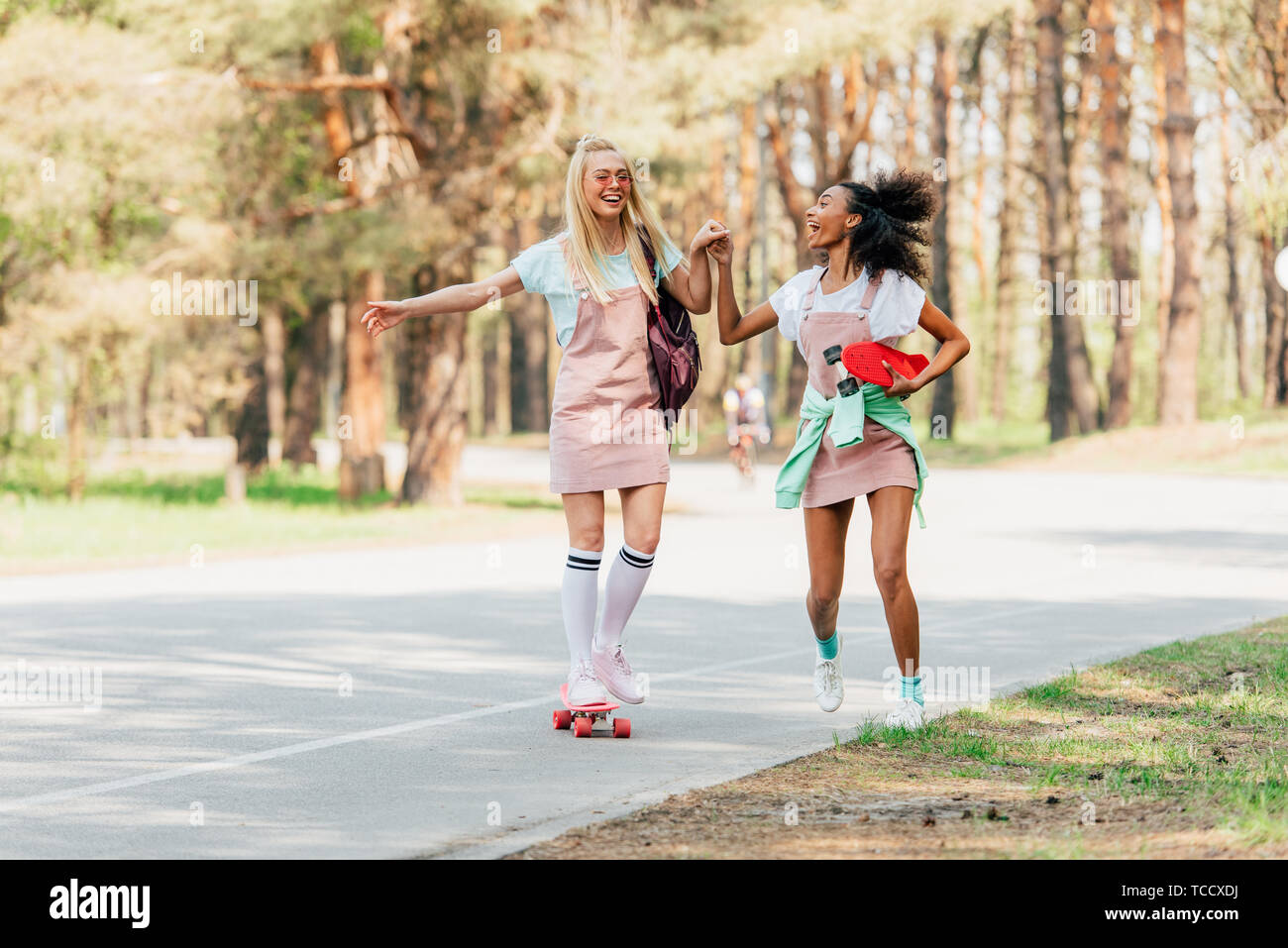 full length view of two smiling multicultural friends holding hands ...