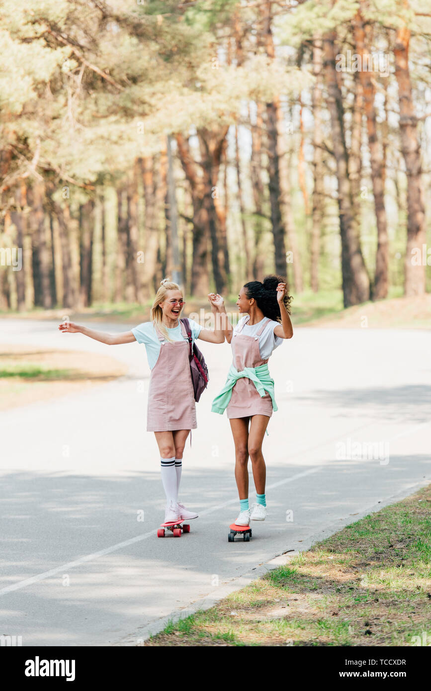 full length view of two smiling multicultural friends holding hands ...